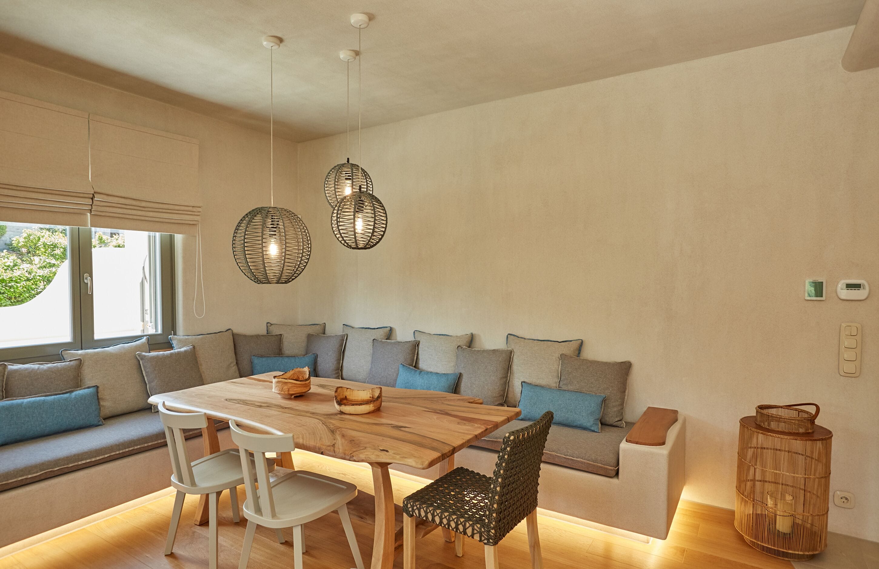Uma área de refeições moderna com mesa de madeira, cadeiras brancas e um banco embutido com almofadas azuis.