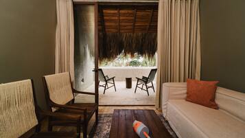 Quarto com sofá, duas cadeiras, mesa de centro e vista para área externa com cadeiras através de uma porta de vidro.