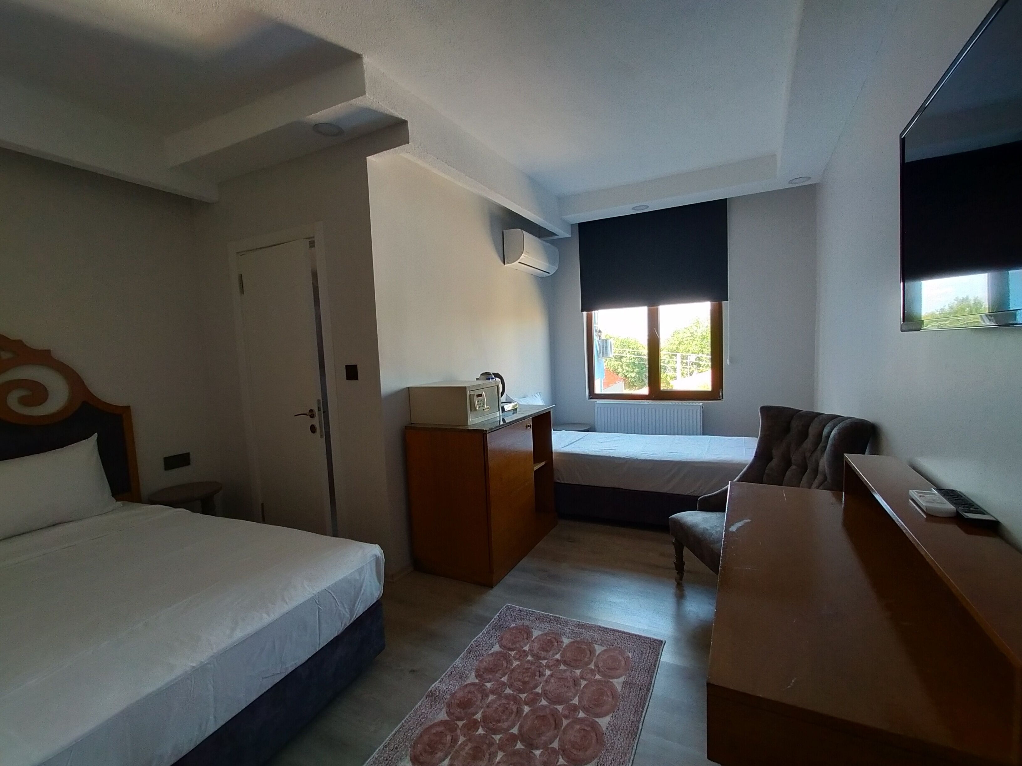 Quarto de hotel com cama, escrivaninha, cadeira, radiador e janela com vista.