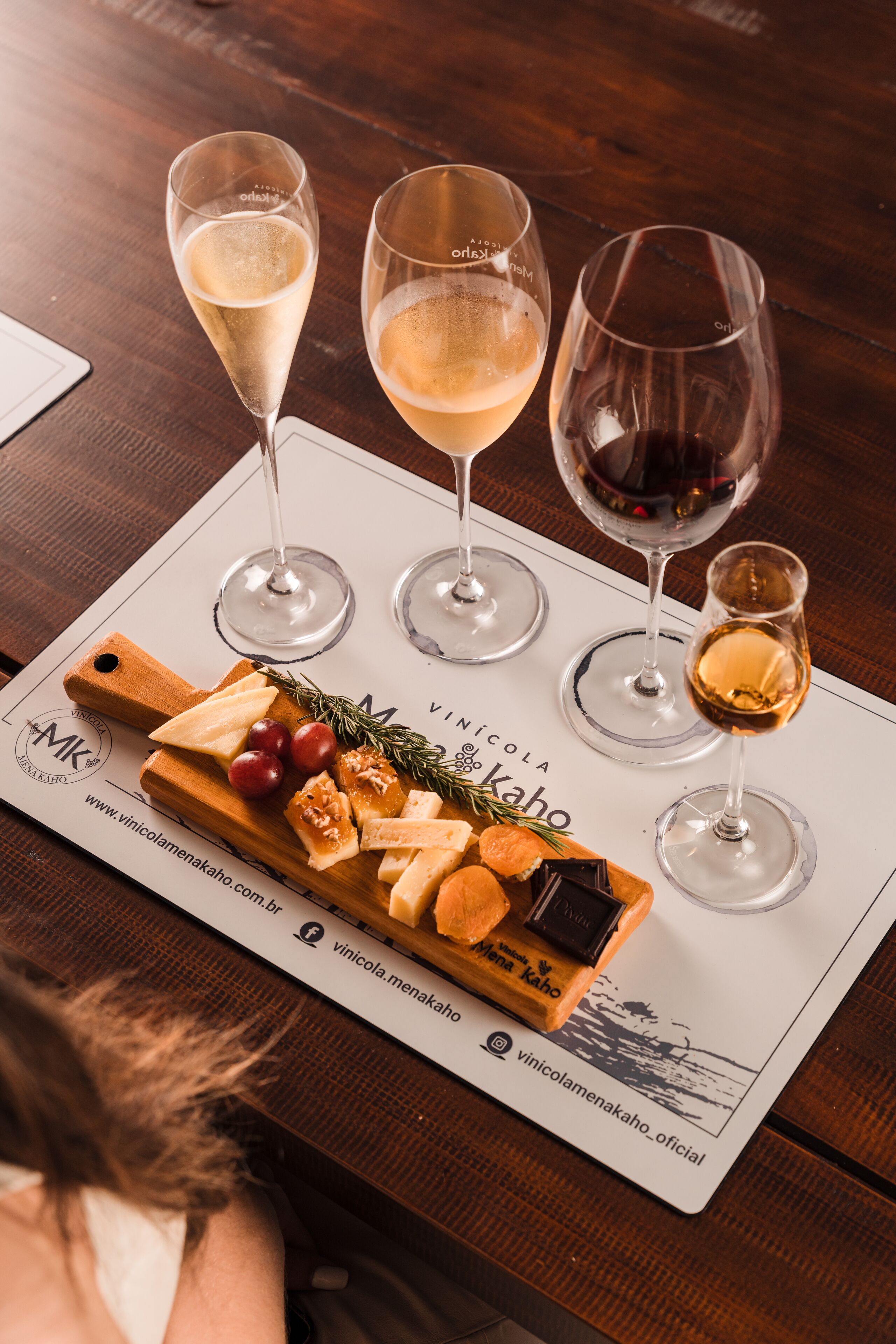 Uma mesa de madeira com degustação de vinho, incluindo taças e uma tábua de queijo e uvas.