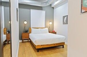 Quarto com cama de madeira, mesas de cabeceira, luminária de parede e um quadro emoldurado.