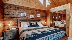 Quarto de cabana de madeira com uma cama grande, paredes de madeira e um claraboia.
