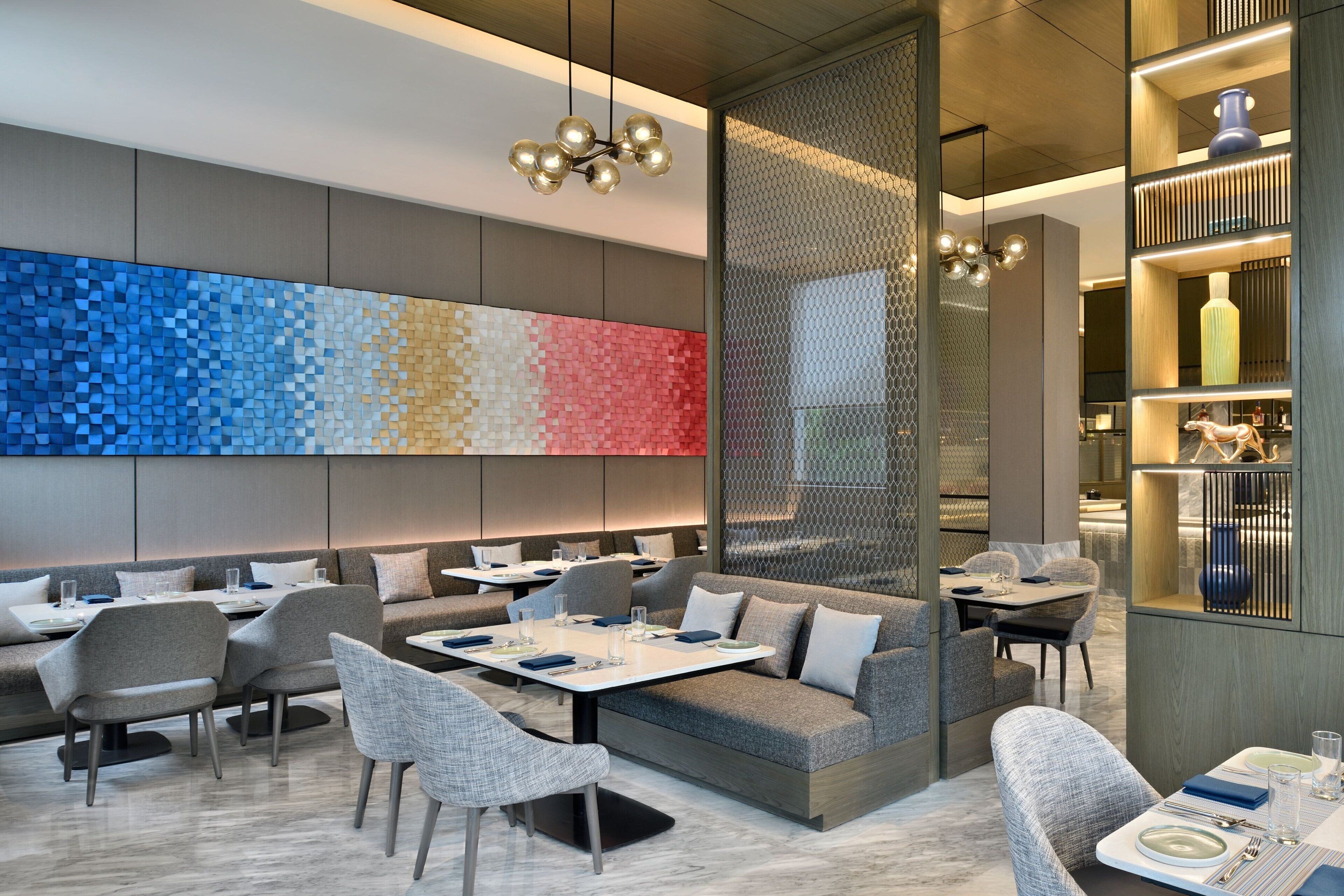 Um restaurante moderno com uma longa mesa de jantar comunitária, lugares individuais e uma obra de arte colorida na parede.