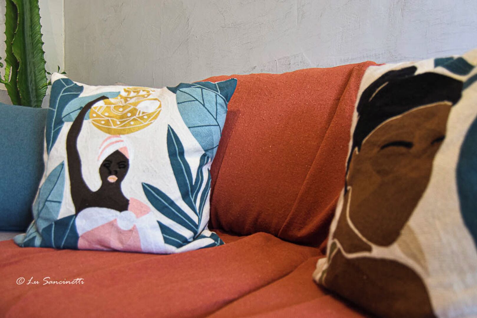 Um sofá com almofadas estampadas e uma planta verde ao fundo.