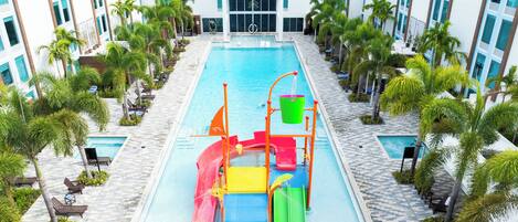 Piscina com toboáguas e área de recreação aquática, cercada por palmeiras e espreguiçadeiras.
