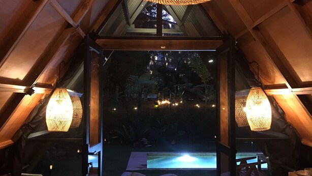 Um quarto de sótão acolhedor e bem iluminado, com uma luminária de palha grande, assentos confortáveis e vista para uma piscina.