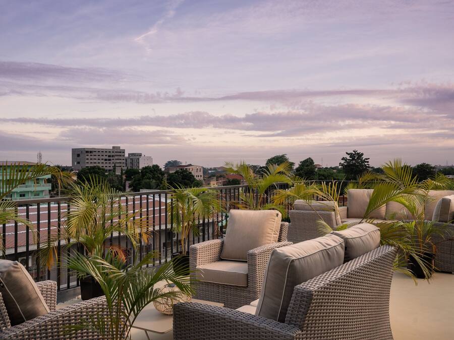 Terraço no telhado com móveis de vime e palmeiras, com vista para a paisagem urbana.