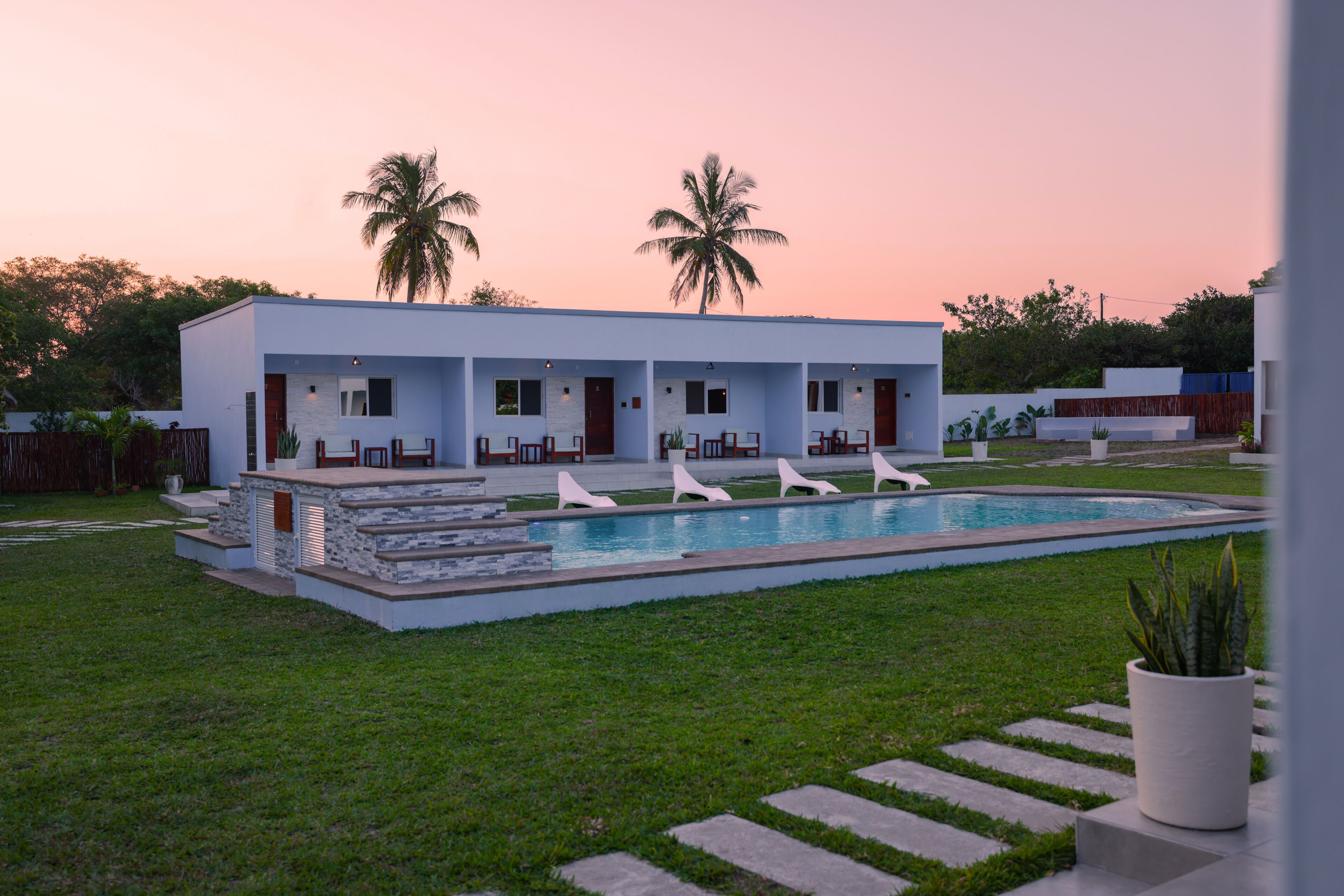 Um edifício moderno com piscina, cadeiras de descanso brancas e palmeiras.
