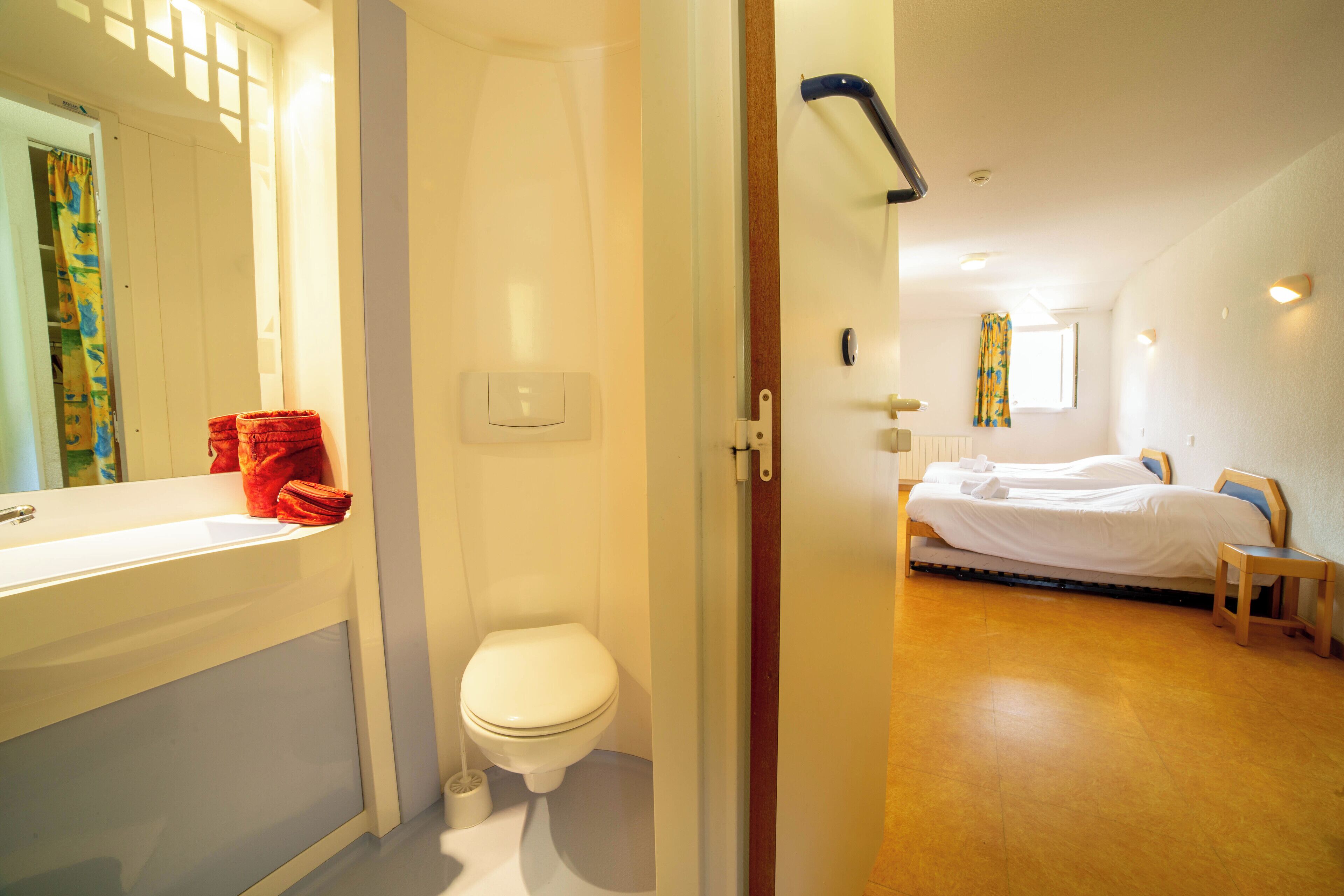 Quarto de hotel com banheiro, cama e piso de madeira.