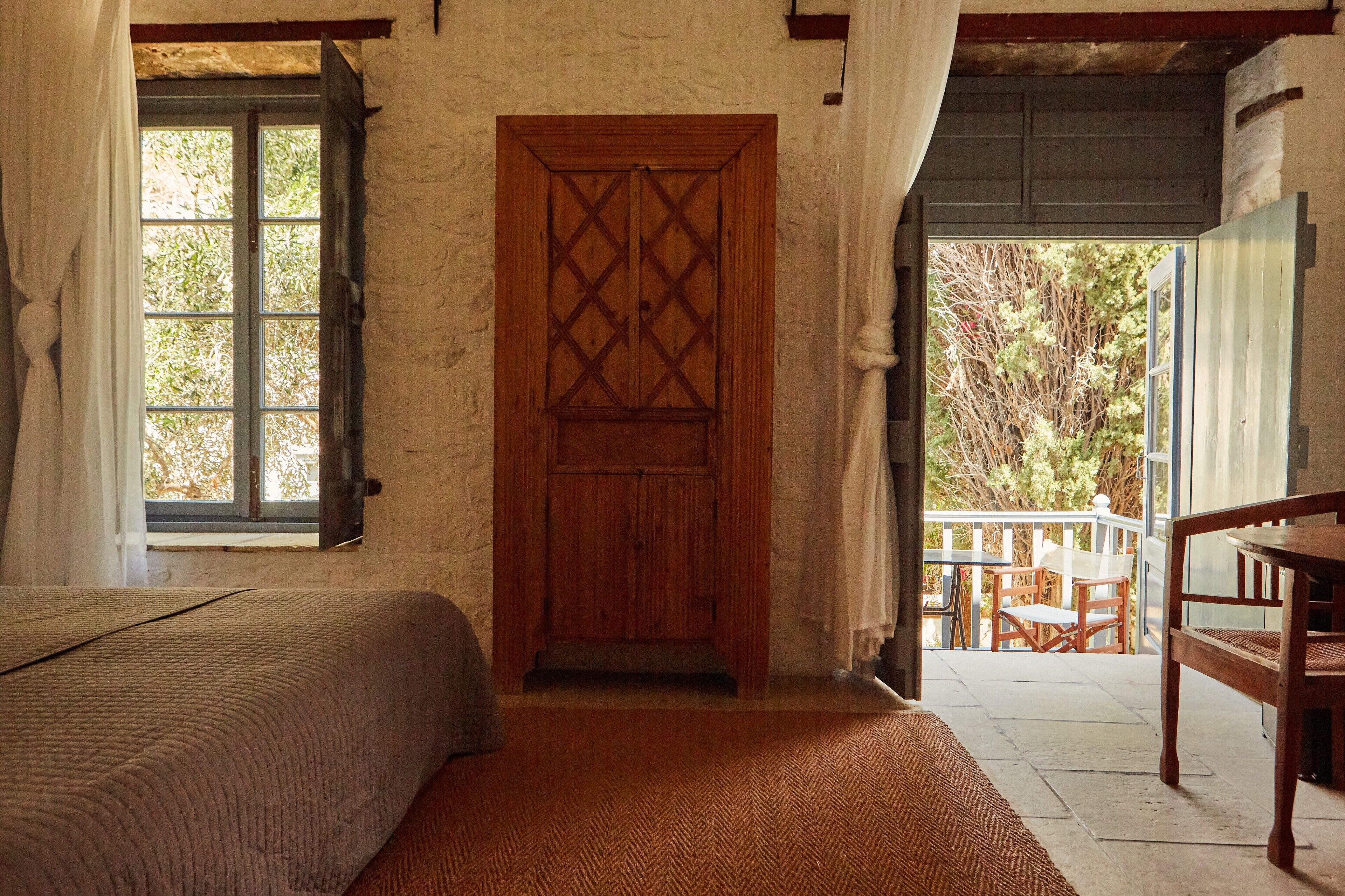 Quarto com uma cama grande, porta de madeira e varanda com mobiliário externo.