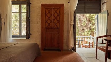 Quarto com uma cama grande, porta de madeira e varanda com mobiliário externo.