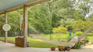 Uma rede sob um alpendre com vista para um jardim exuberante e árvores.