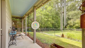 Uma área de varanda coberta com um letreiro escrito 'Good Vibes', móveis de exterior e vista para um jardim cercado com árvores.