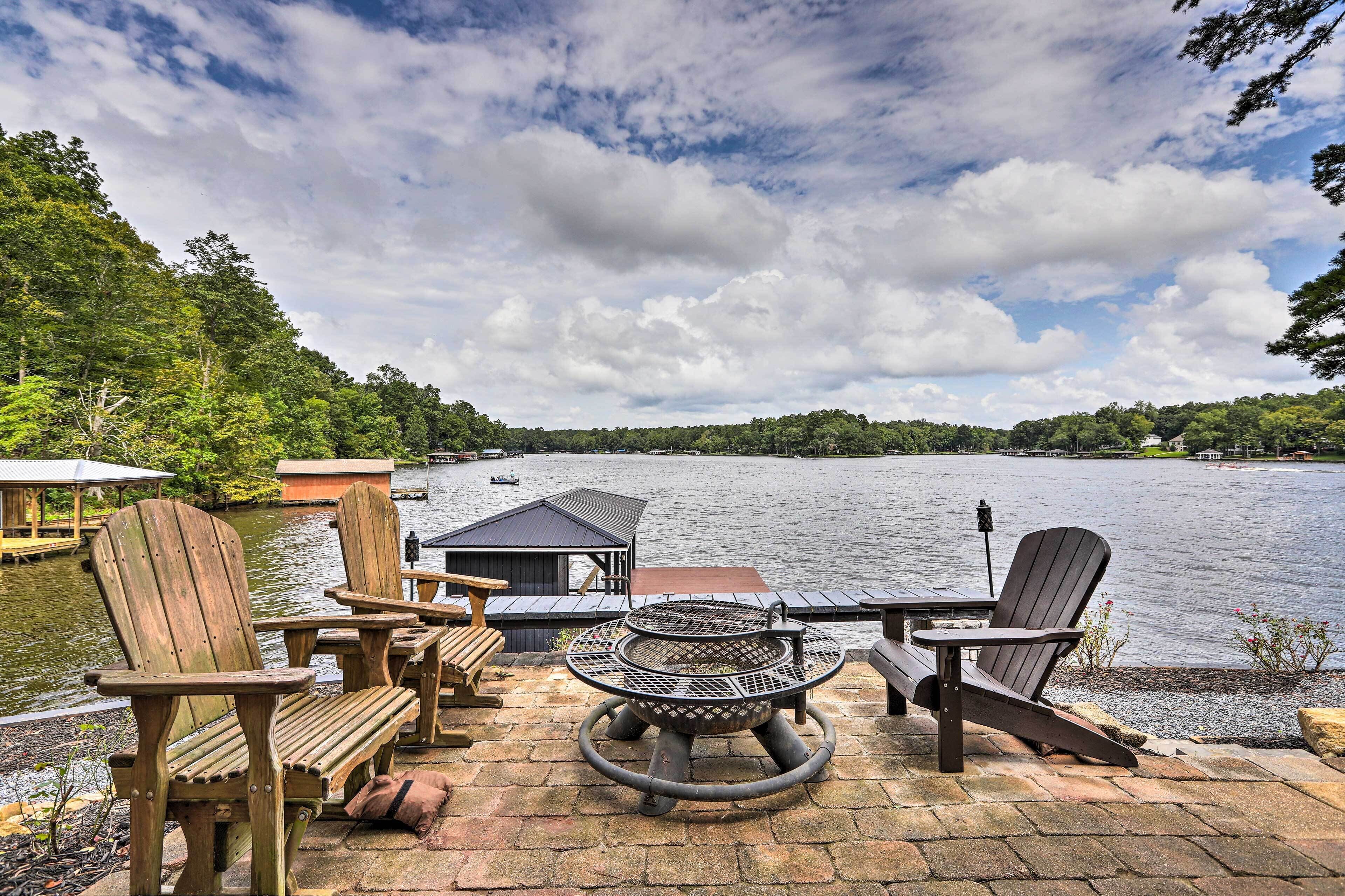 Um deck à beira do lago com cadeiras Adirondack, uma fogueira e vista para o lago.
