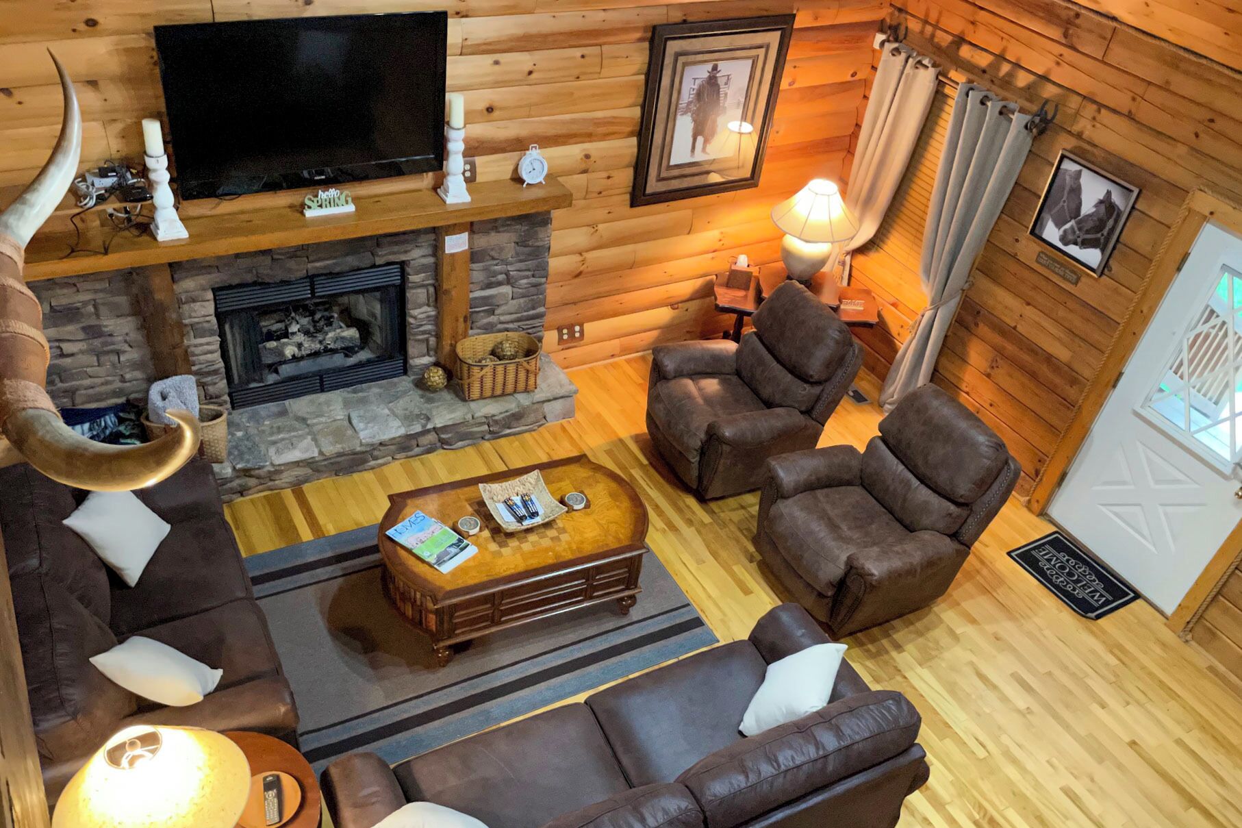 Interior de cabana de madeira com lareira de pedra, sofás de couro, televisão e moldura de quadro pendurada.