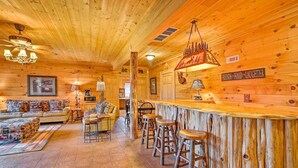 Interior acolhedor de uma cabana com balcão de madeira, área de estar e lareira.