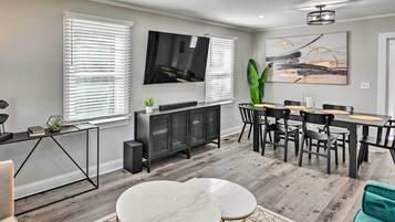 Uma sala de estar moderna com área de jantar, apresentando uma televisão, um armário e uma mesa de jantar com cadeiras.
