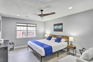 Quarto com cama, escrivaninha, cadeira, mesa de cabeceira, abajur, ventilador de teto e janela.