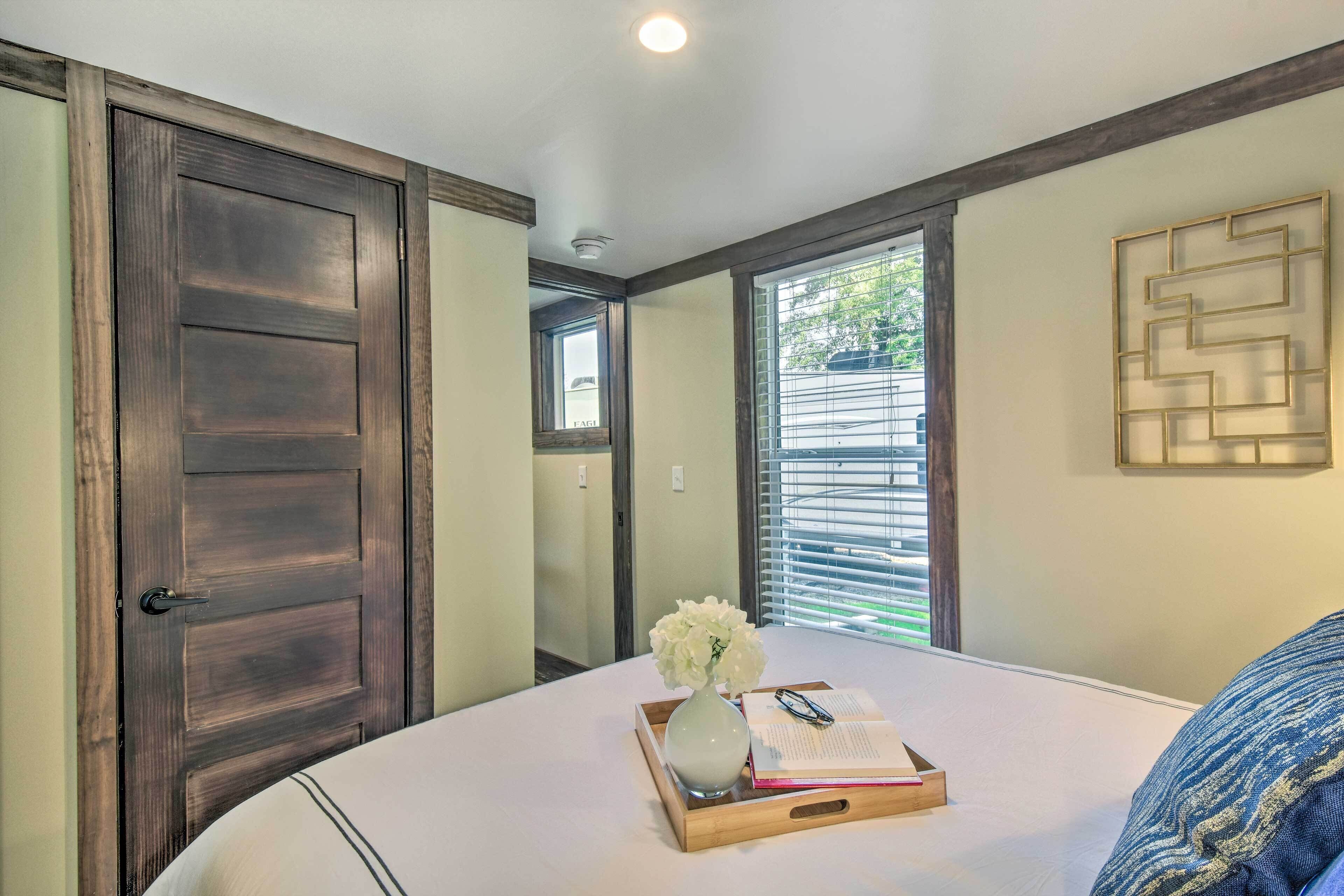 Quarto com uma cama grande, porta de madeira, janela com persianas e um objeto decorativo na parede.