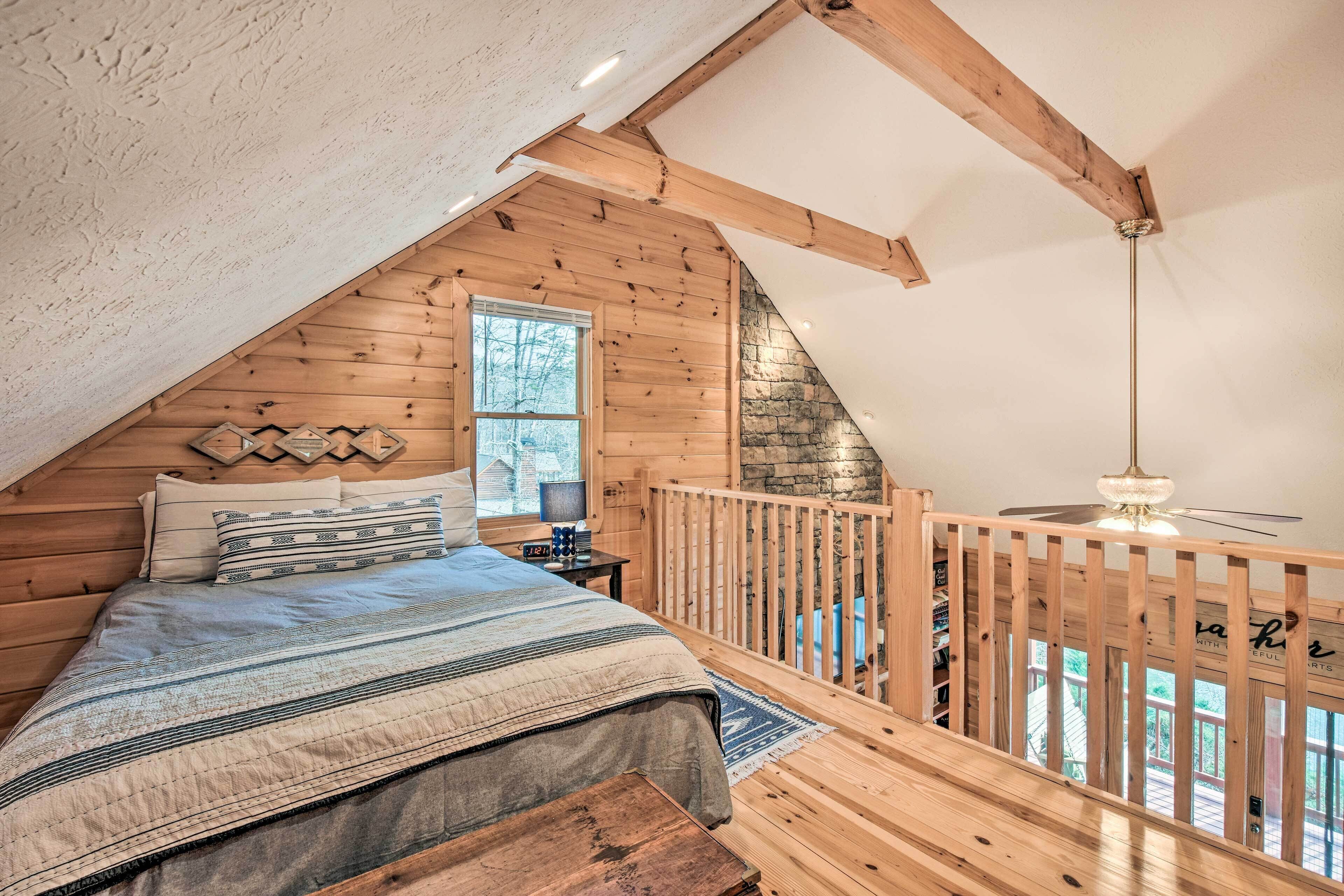 Um quarto de sótão acolhedor, com teto inclinado, vigas de madeira, uma cama com coberta listrada, uma mesa de cabeceira e vista para o exterior.