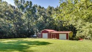 Um celeiro vermelho com porta de garagem branca, cercado por um campo gramado e árvores densas.