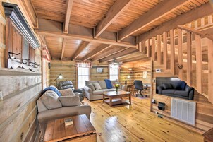 Interior acolhedor de uma cabana de toras, com paredes de madeira, um sofá, uma mesa de centro e uma TV fixada na parede.
