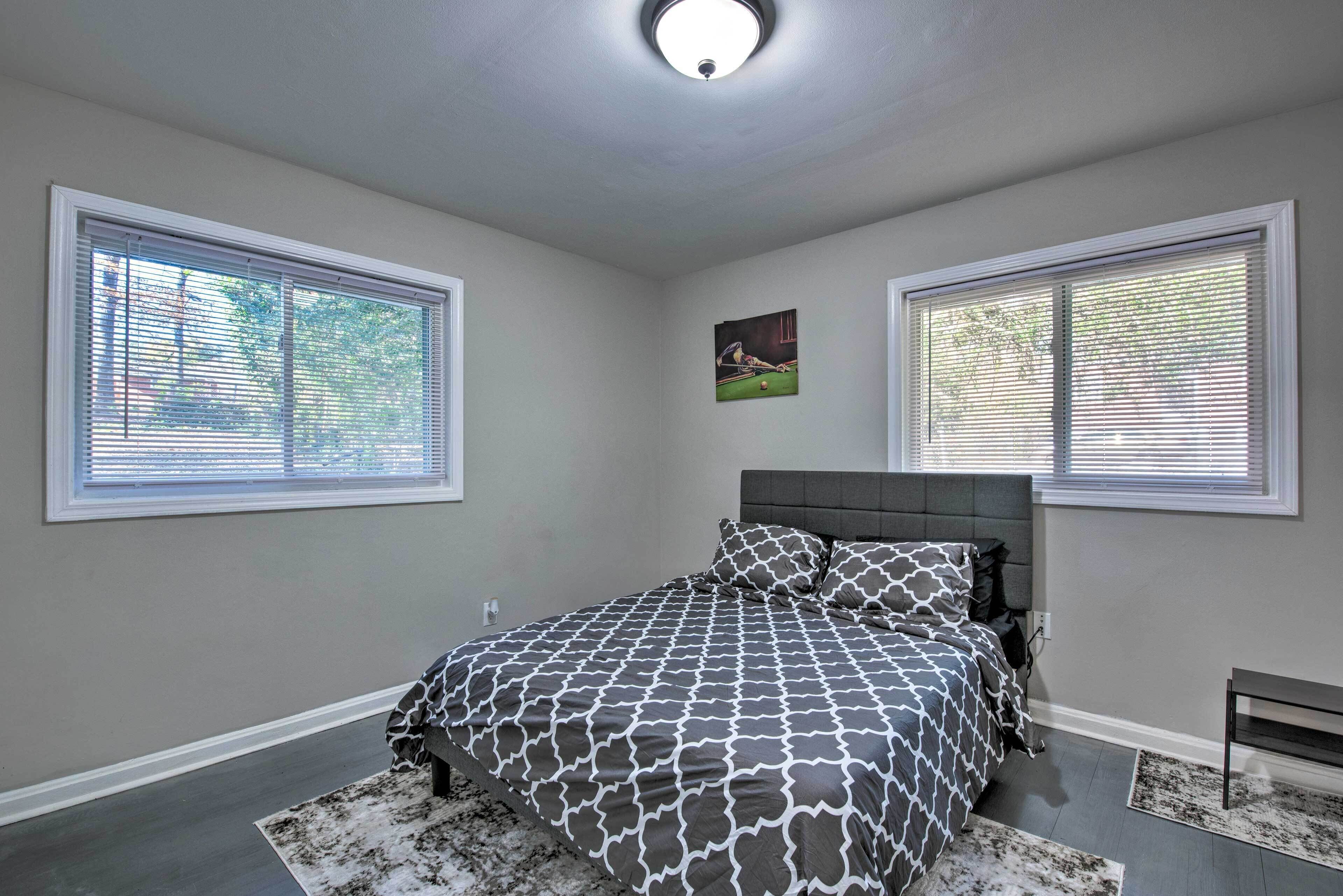 Quarto com uma cama, duas janelas, uma luminária no teto e um quadro na parede.