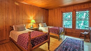 Um quarto com painéis de madeira, duas camas, uma mesa de cabeceira, uma cadeira e uma janela grande.