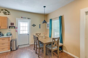 Uma área de refeições com uma mesa e cadeiras de madeira, uma lixeira e uma porta com uma placa acima.