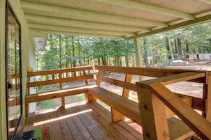 Um deck de madeira com bancos, uma porta de vidro e vista para uma floresta.