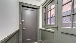 Um corredor com uma porta escura, uma janela com vários painéis e um tapete texturizado.