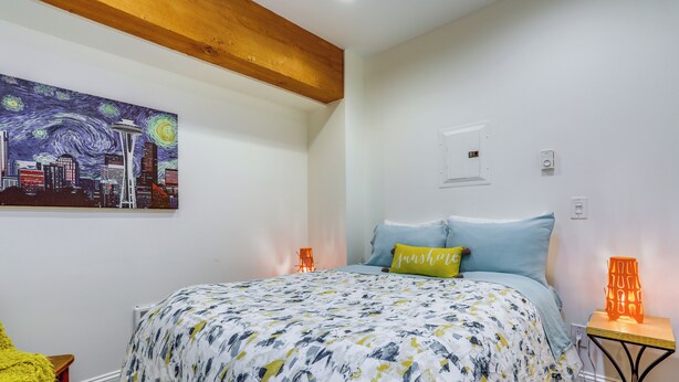 Quarto com cama, quadro, mesa de cabeceira e abajur.