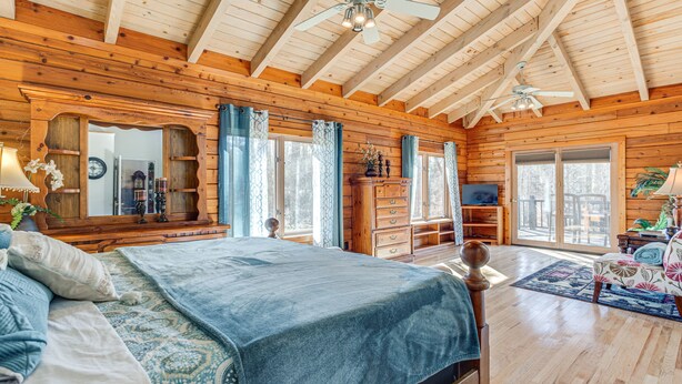 Quarto de cabana de tronco com cama, cômoda e ventoinha no teto.