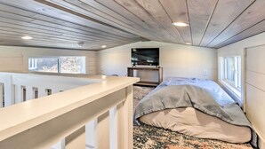 Quarto com cama de solteiro, teto de madeira, televisão em suporte e uma janela.