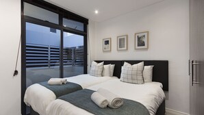 Quarto de hotel moderno com duas camas, varanda e obras de arte na parede.