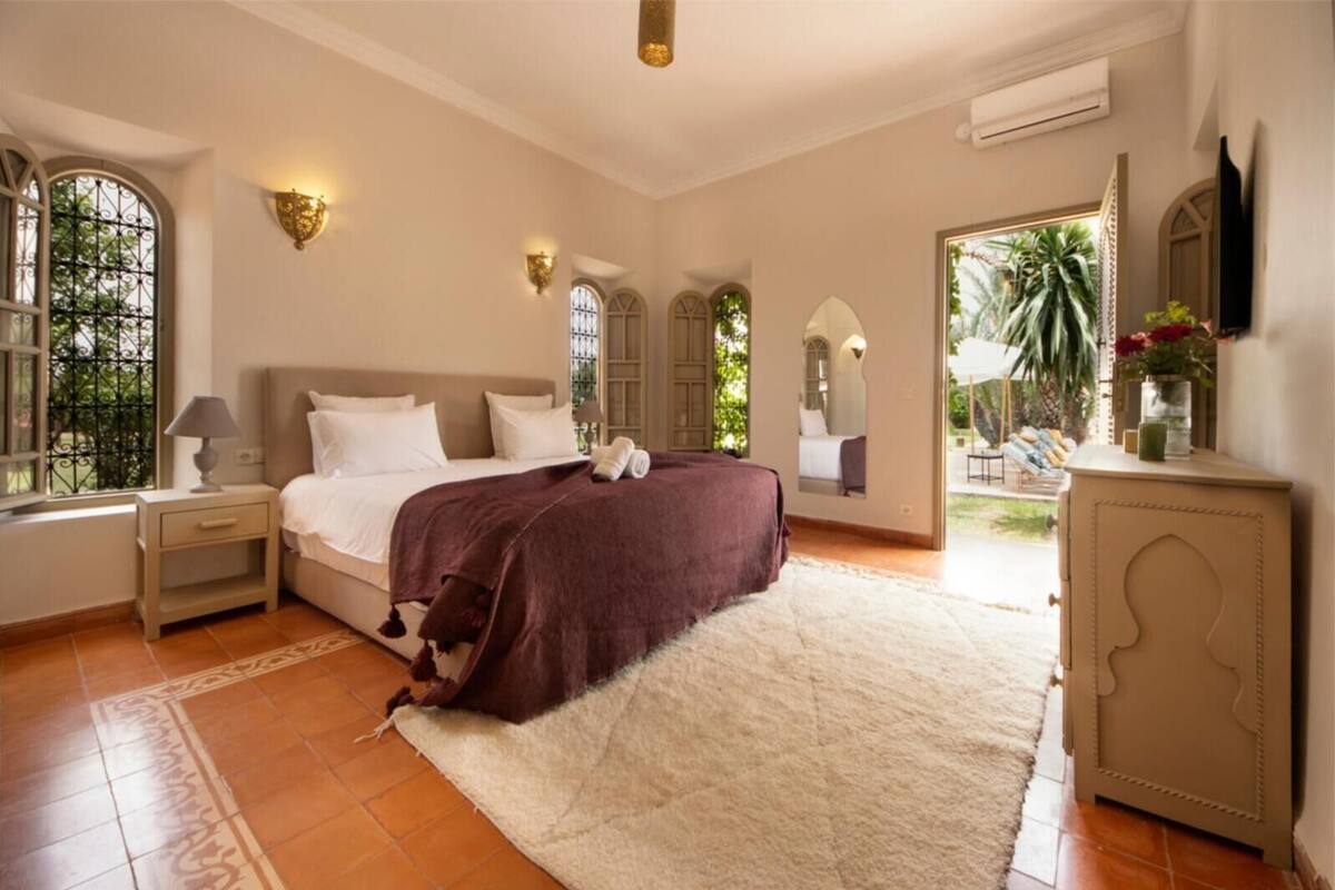 Quarto com cama, mesas de cabeceira, cômoda e uma janela grande com vista para o exterior.