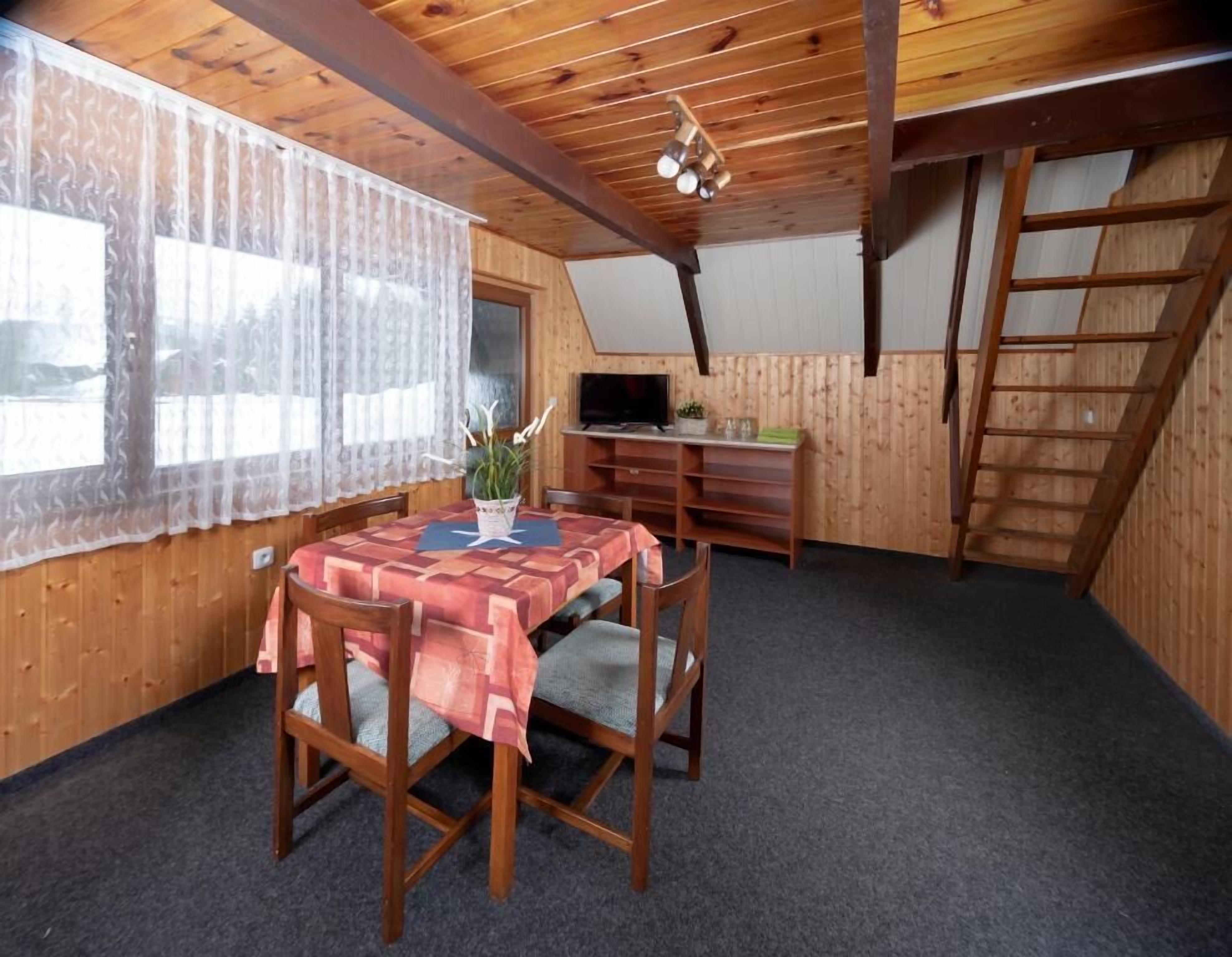 Um quarto acolhedor com teto de madeira, uma mesa de jantar com cadeiras, uma televisão e uma estante de livros.