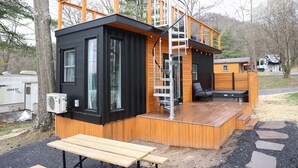 Uma cabana moderna com um deck de madeira, uma escada em espiral e uma área de varanda.