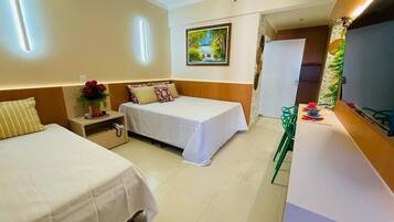 Quarto de hotel com duas camas, uma escrivaninha com cadeira, um quadro na parede e zona de duche.