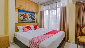 Quarto de hotel com uma cama grande, cabeceira de madeira, uma pintura de cavalos e uma janela com cortinas.
