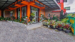 Um edifício com entrada coberta, rodeado por plantas em vasos e um caminho de acesso de cascalho.