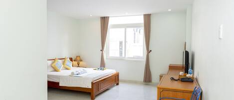 Quarto com cama, escrivaninha, cadeira, televisão e janela com cortinas.
