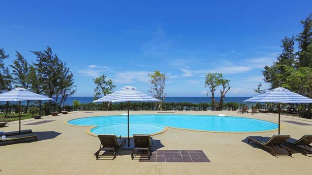 Piscina com espreguiçadeiras e guarda-sóis, cercada por árvores e um céu claro.