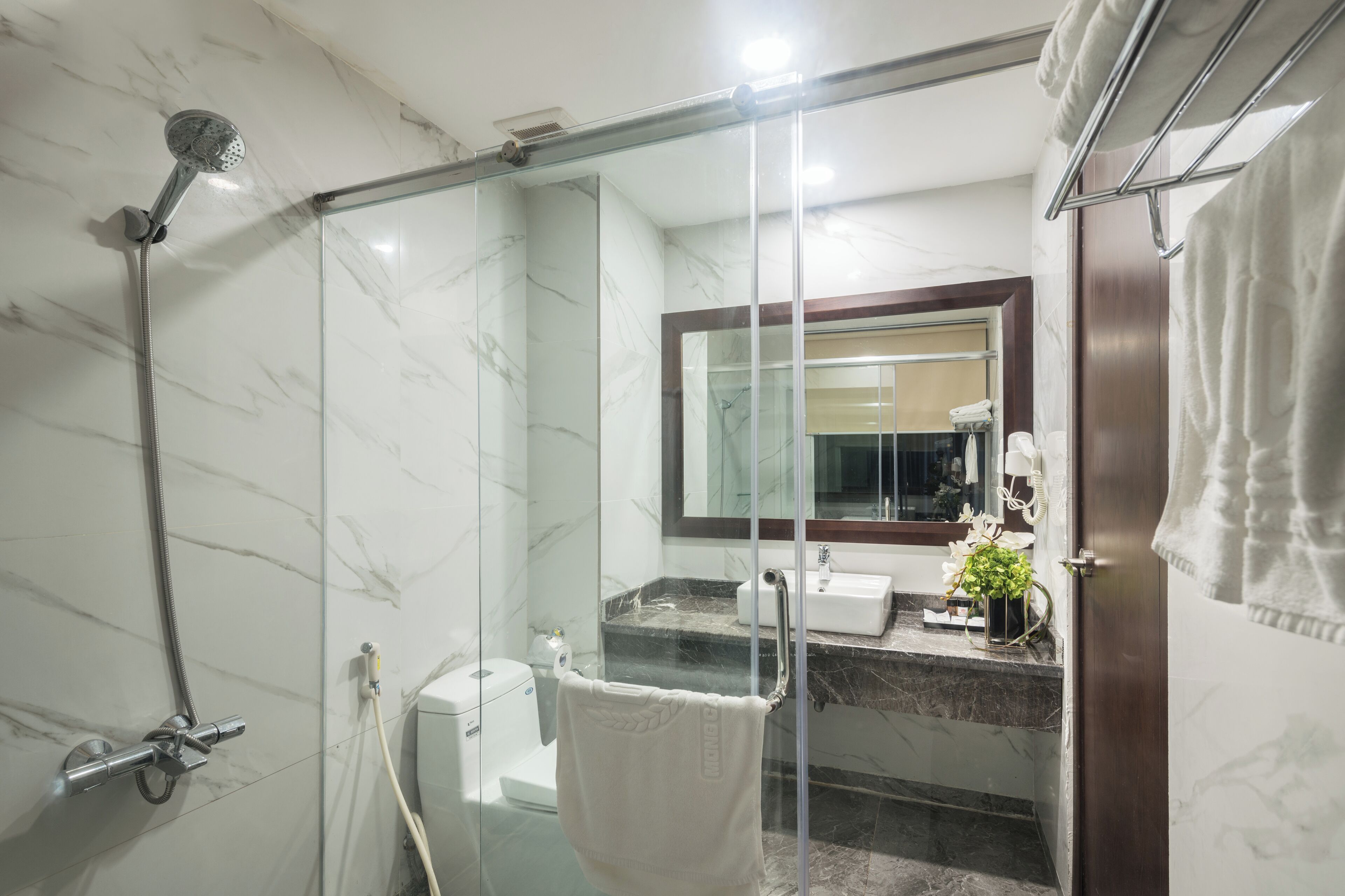 Um banheiro moderno com chuveiro envidraçado, paredes de mármore, pia com espelho e porta-toalhas.
