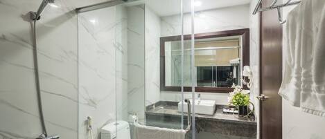 Um banheiro moderno com chuveiro envidraçado, paredes de mármore, pia com espelho e porta-toalhas.