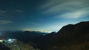 Vista noturna de uma paisagem montanhosa com um vale e luzes de cidade ao longe.