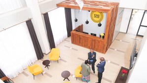 Um hall de entrada com balcão de recepção, diversas áreas de estar e um grande janelão com cortinas.