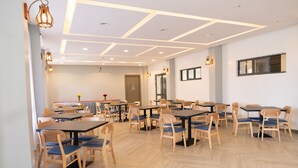 Uma ampla área de jantar com várias mesas e cadeiras, destacando um design moderno no teto e iluminação ambiente.