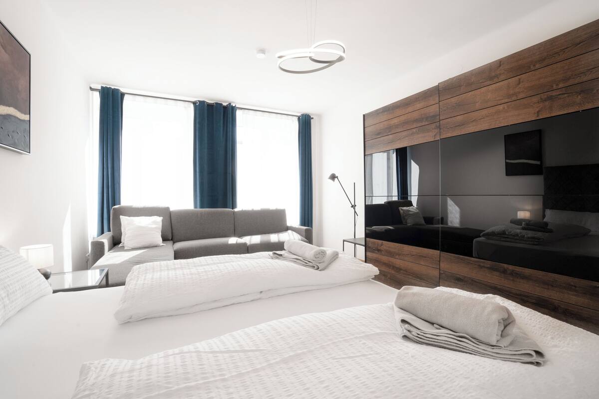Quarto de hotel moderno com uma cama grande, um sofá, uma escrivaninha e uma televisão.