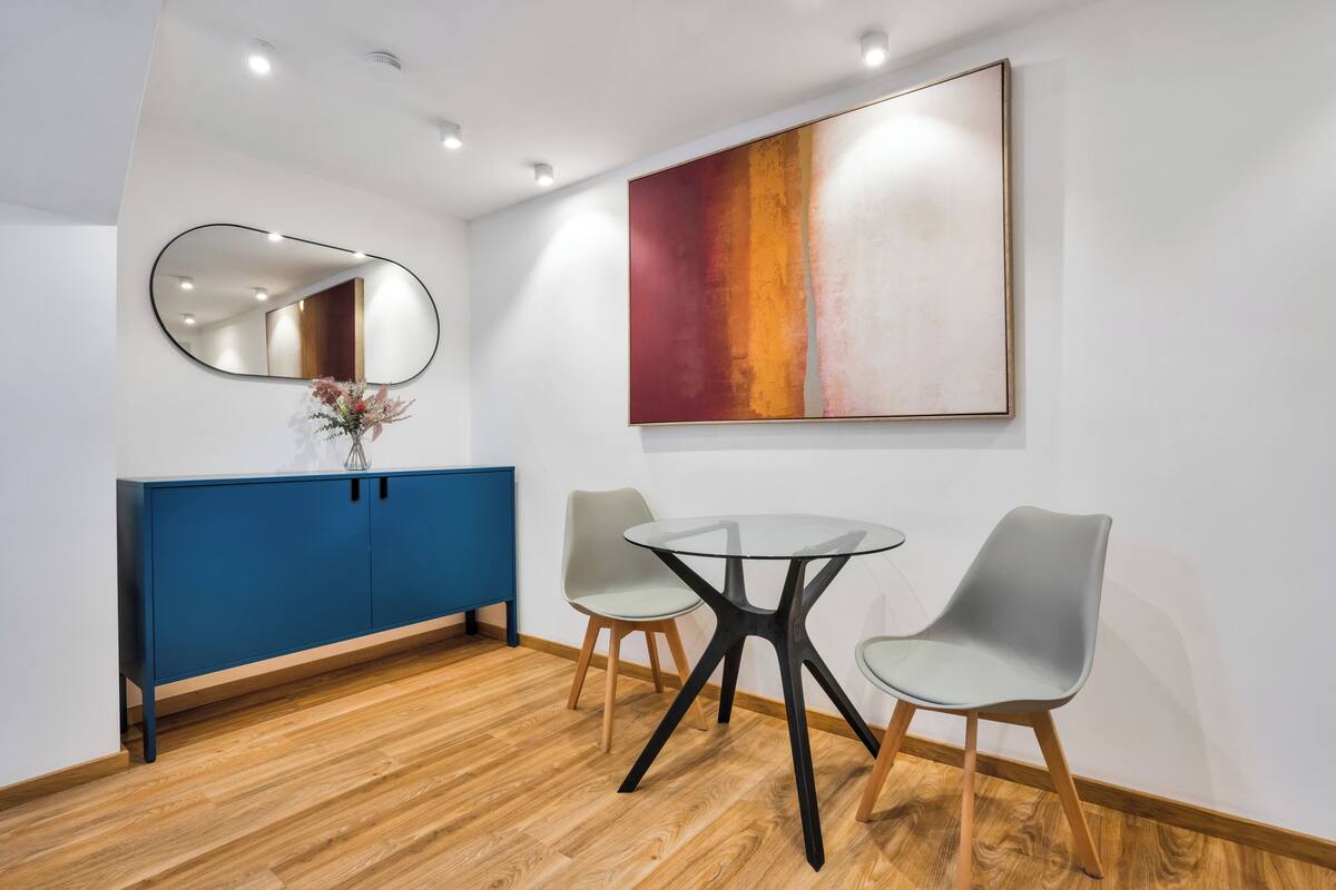 Uma sala de reuniões moderna com um armário azul, uma mesa redonda de vidro e duas cadeiras cinzas.